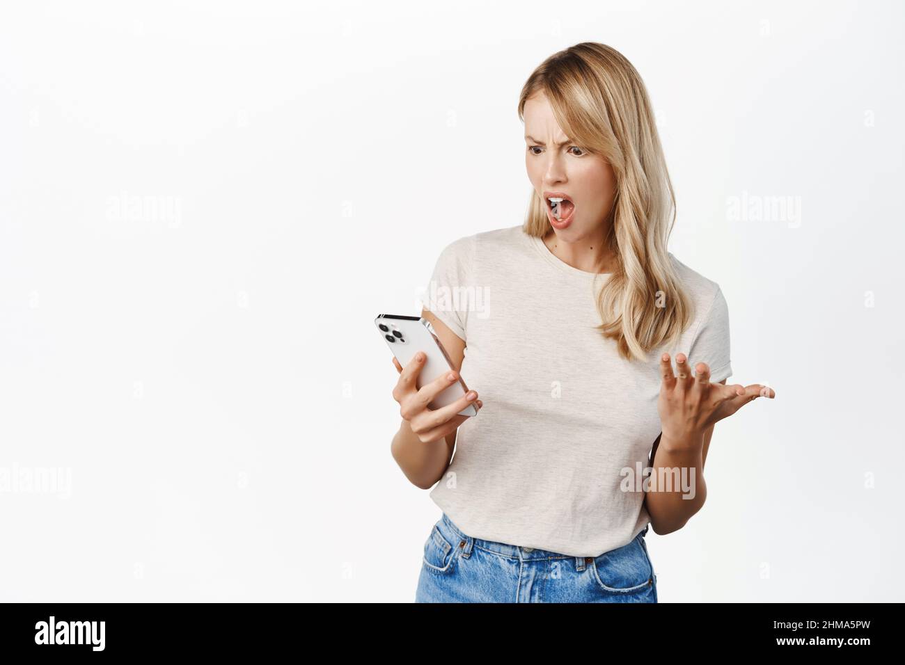 Angry young woman screaming, complaining at mobile phone, looking frustrated at cellphone ...