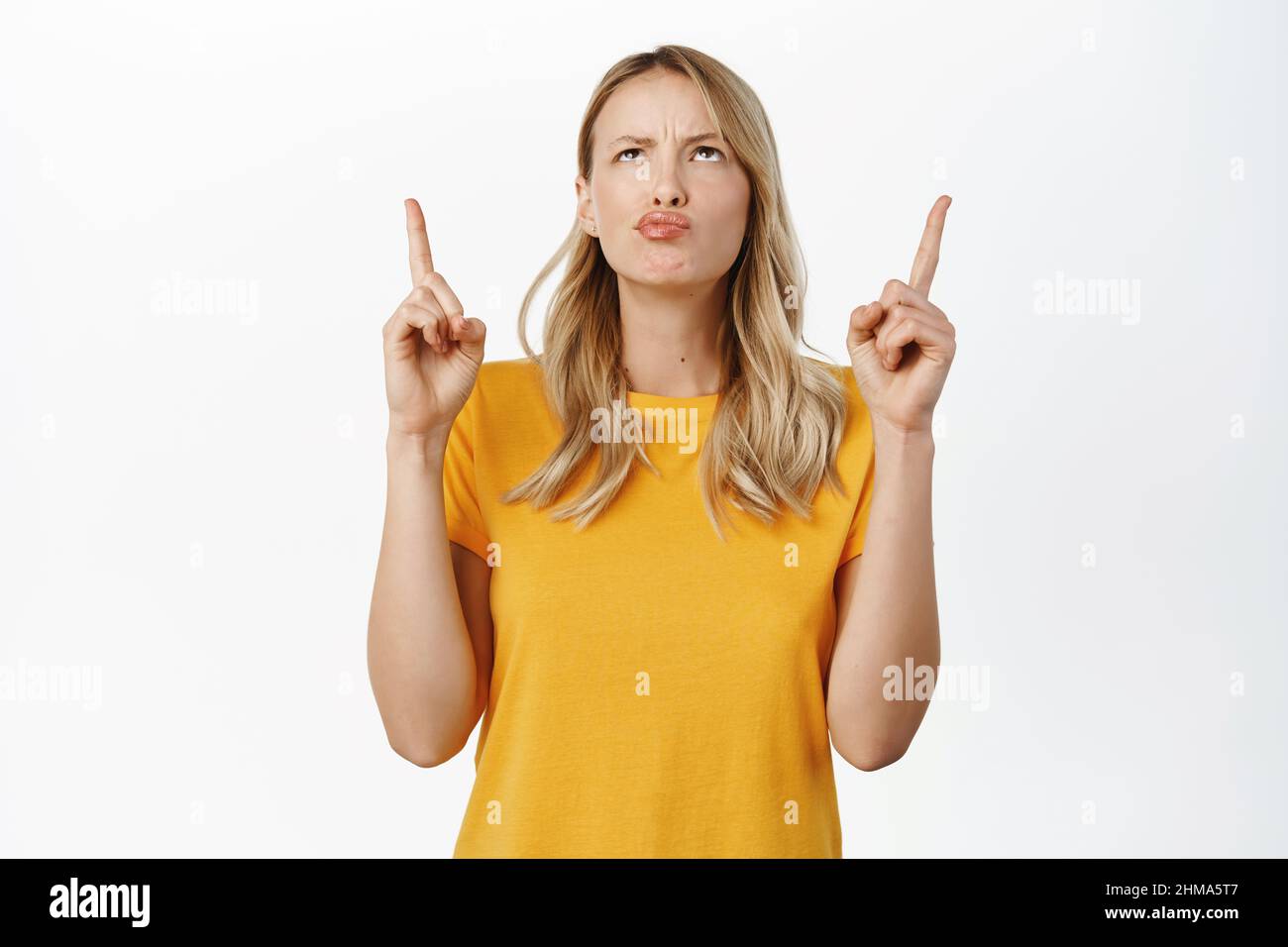 Suspicious young woman grimacing, pointing finger up, expressing doubt ...