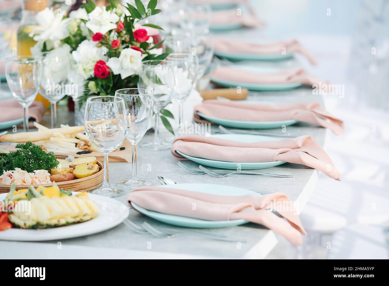 Curved banquet table with plates and pink napkins outdoors. Low angle ...