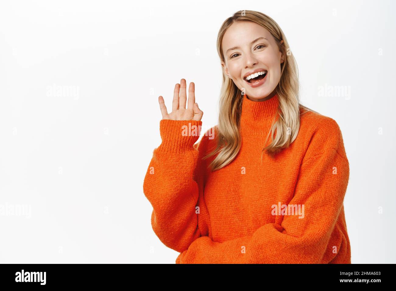Friendly happy blond girl say hello, waving hand and smiling, greeting ...