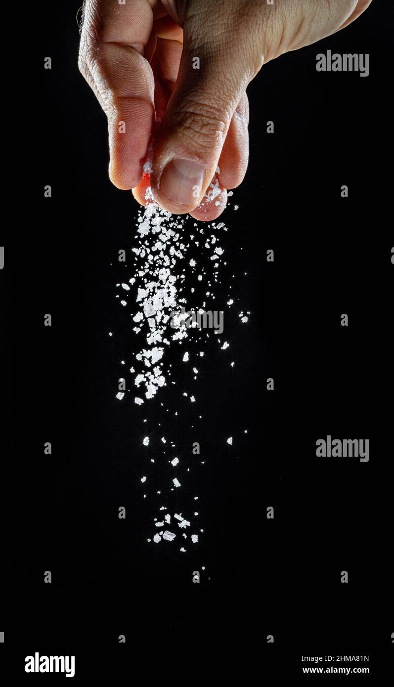 Male hand sprinkling edible salt at black background Stock Photo - Alamy