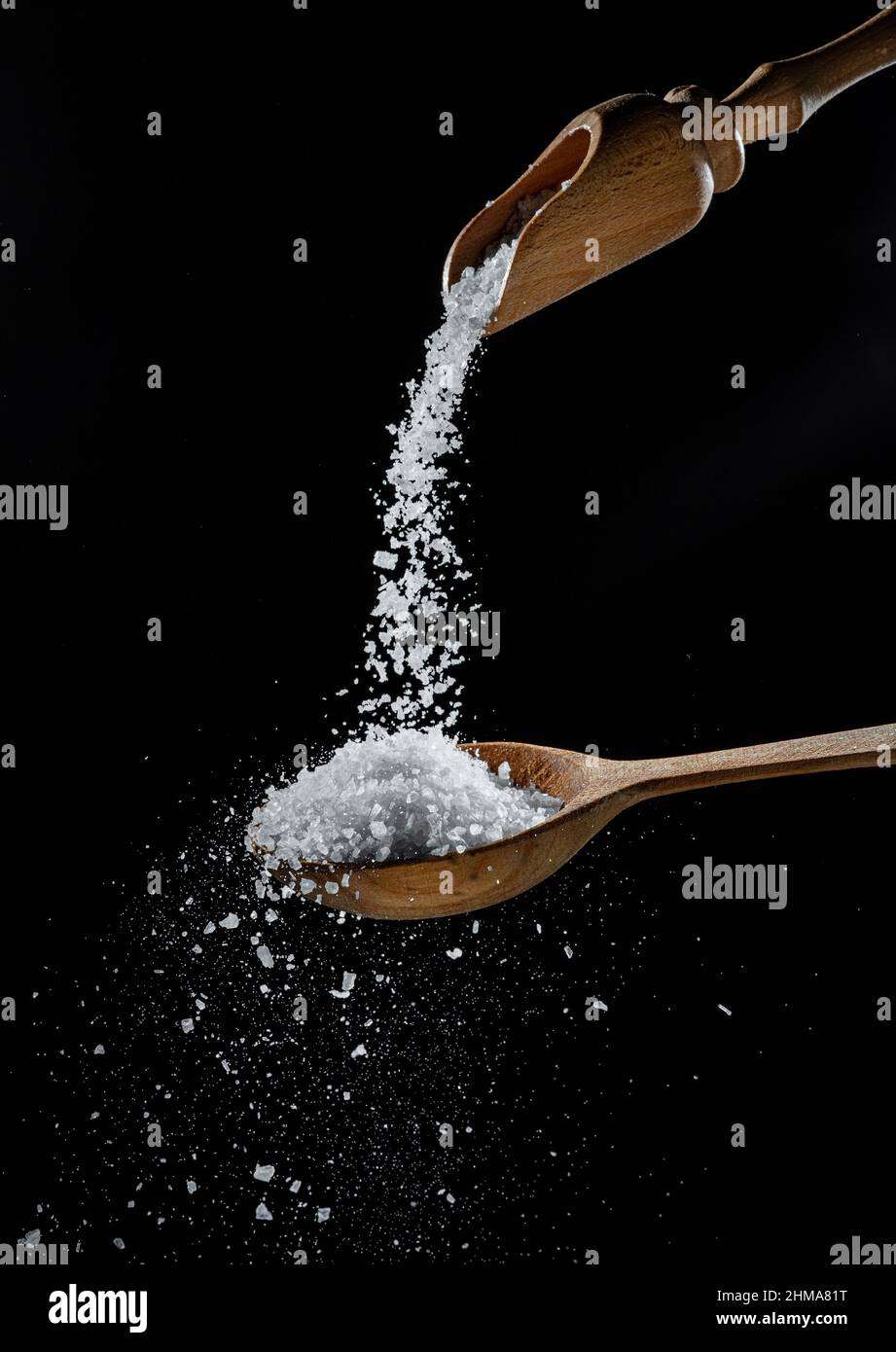 Edible salt crystals falling down into the wooden spoon at black ...