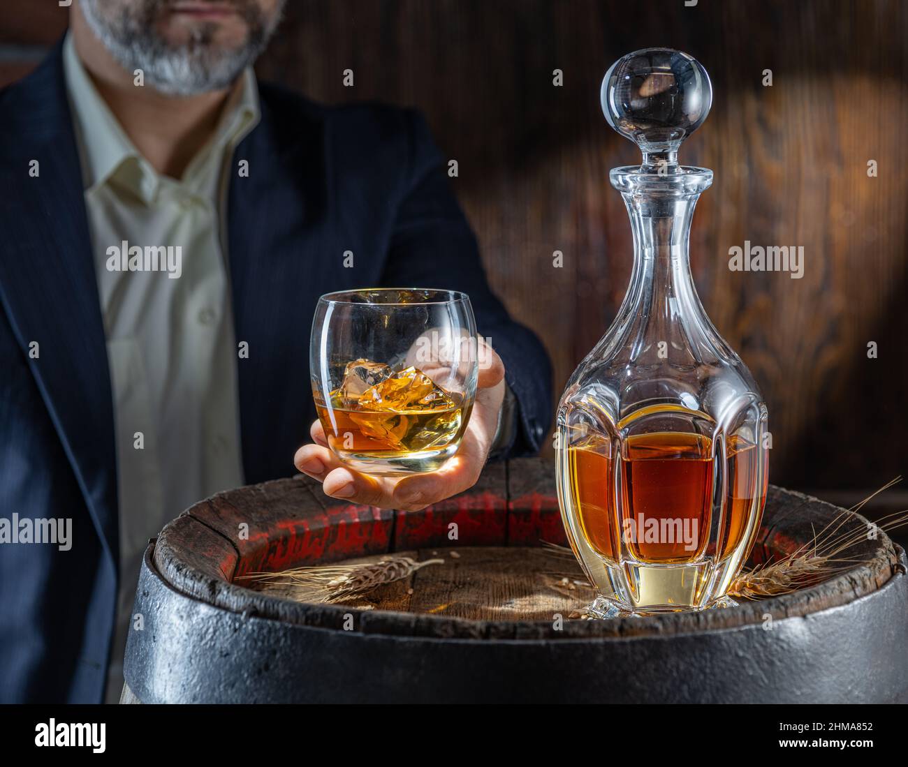 Whisky tasting. Man sits in front of a barrel with a decanter and a ...