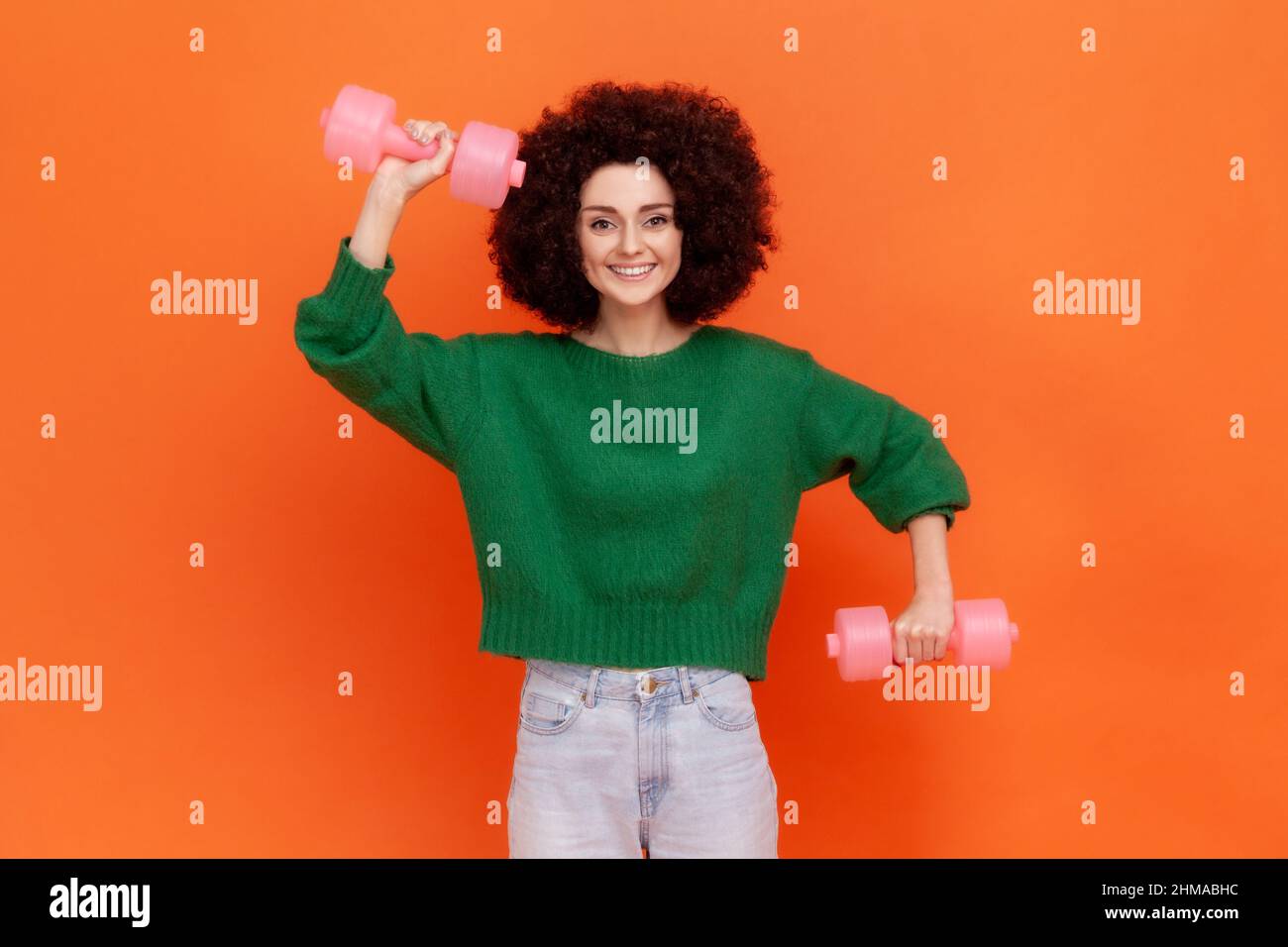 Happy positive sporty woman with Afro hairstyle wearing green casual style sweater doing ...