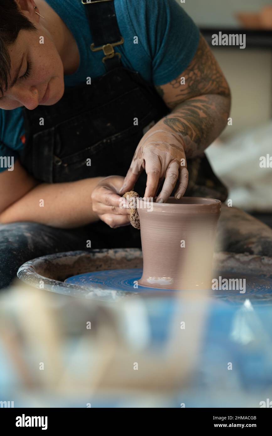Potter smoothing a clay pot on a pottery wheel with a sponge Stock ...