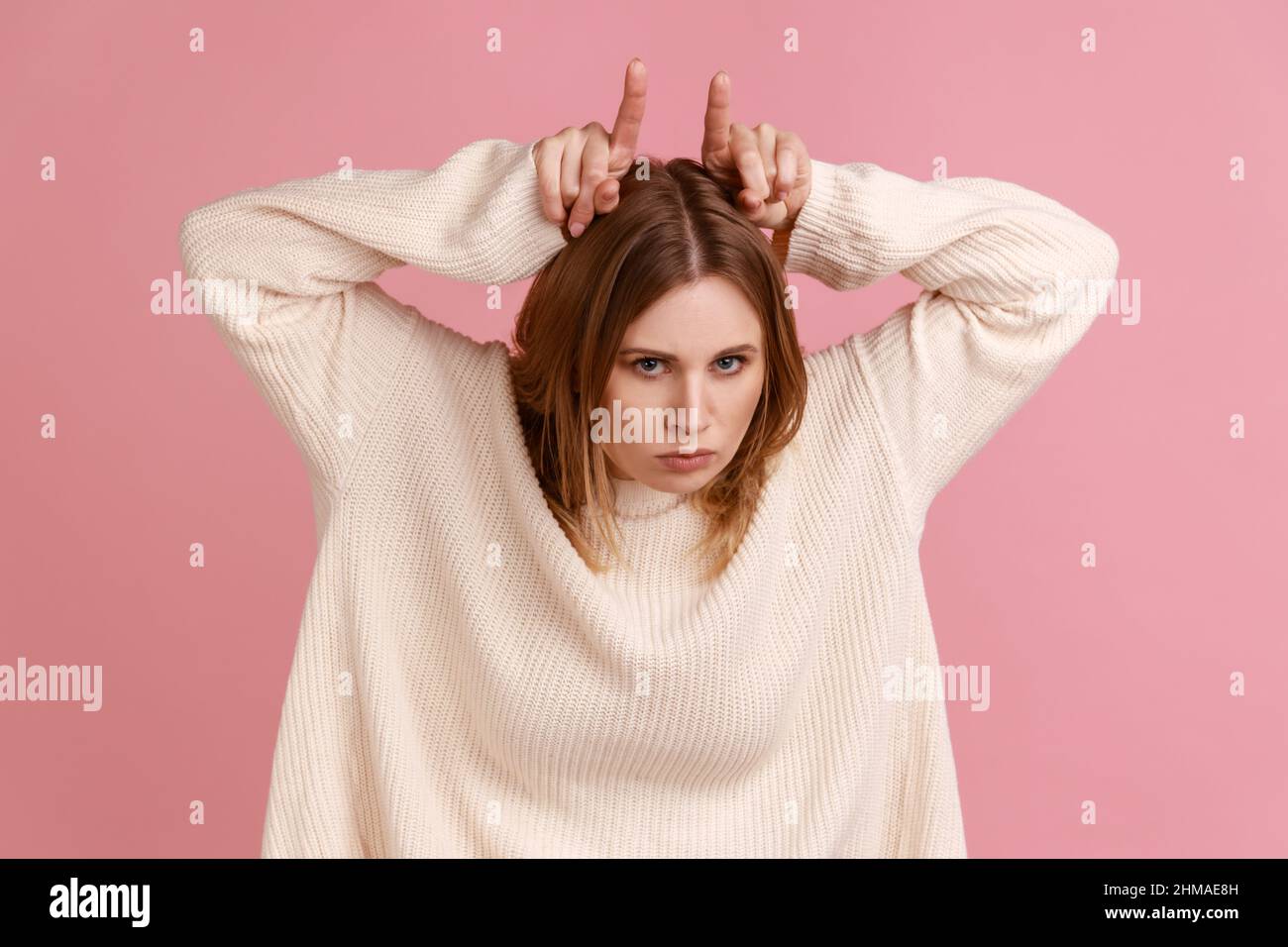 Portrait of aggressive blond woman making bull horns gesture over her ...