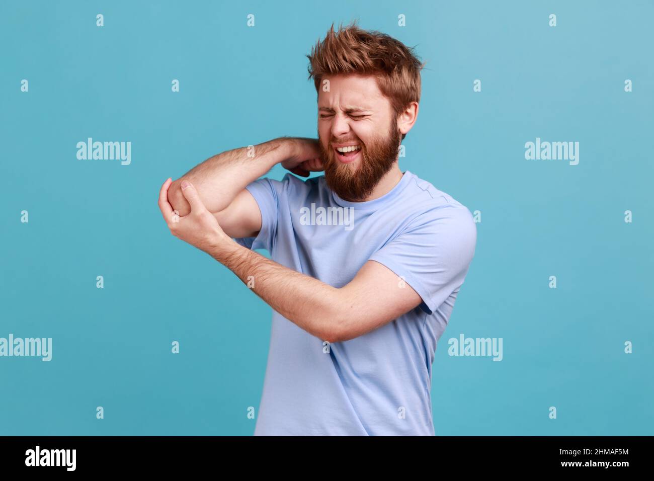 Portrait of bearded man massaging aching elbow, frowning from acute ...