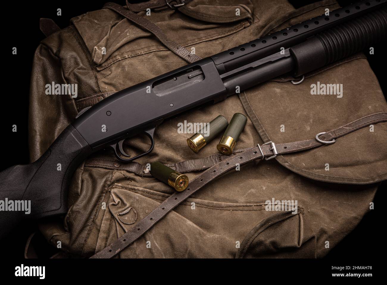 A black 12-gauge pump-action shotgun and ammo are on a canvas backpack ...