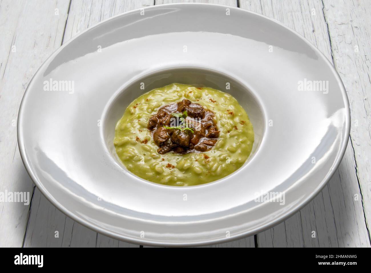 Vegetable risotto with duck stew, in a white plate on white wooden ...