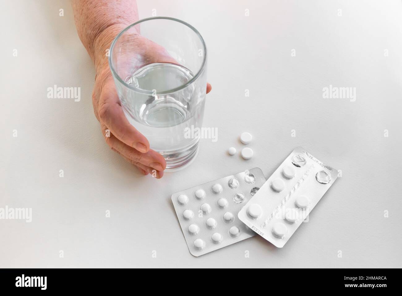 Hands of an elderly person with pills, packaging of medication. Glass ...