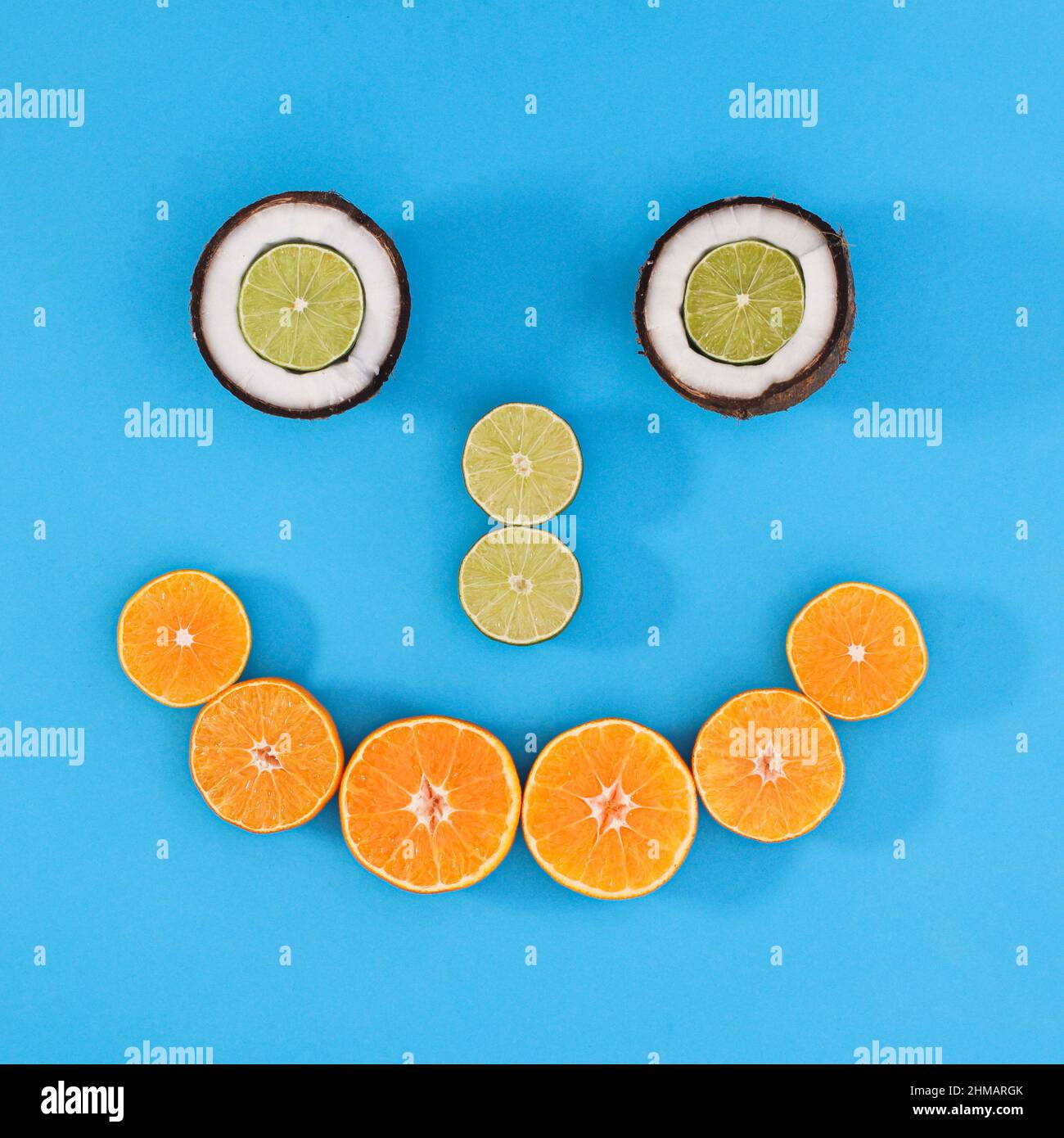 Creative smiley face made of citrus fruits and coconut on cyan or blue ...