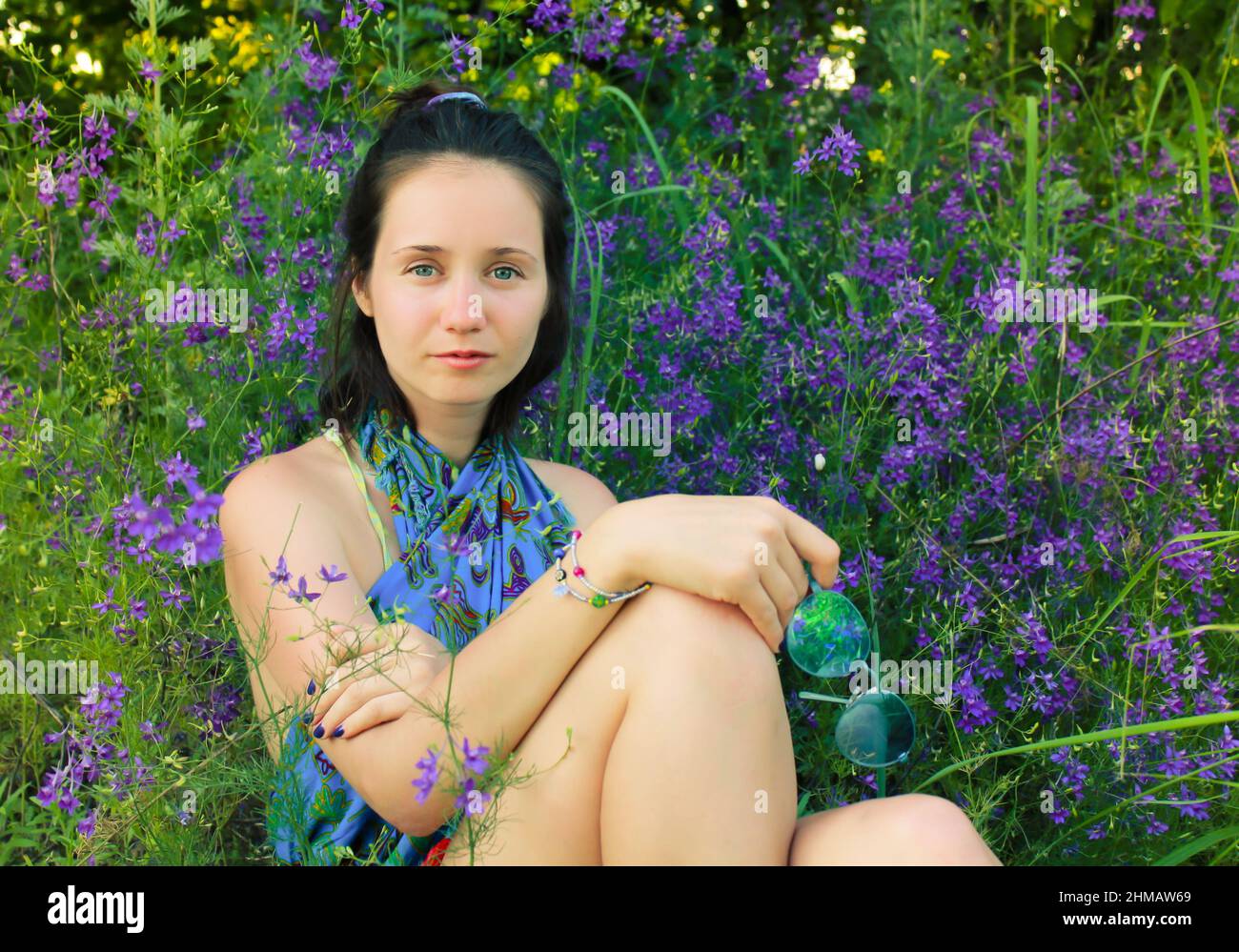 Beautiful white brunette hippie girl sitting in lawn among purple ...