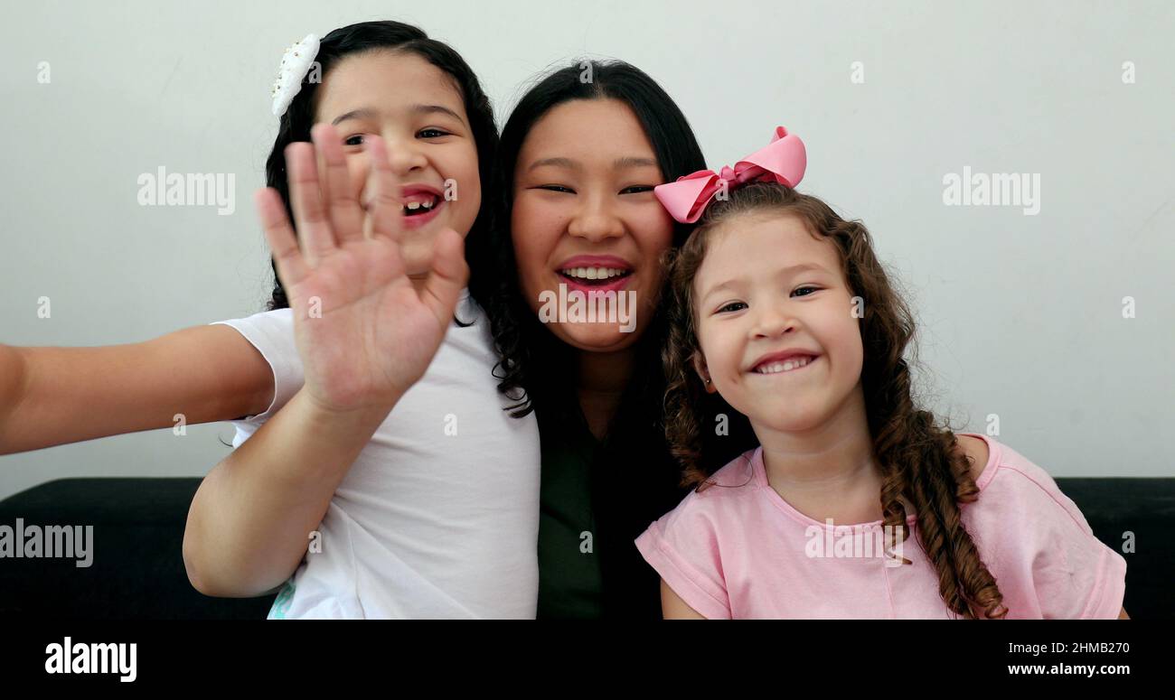 Asian mother waving hello to camera holding multi-ethnic little girls ...
