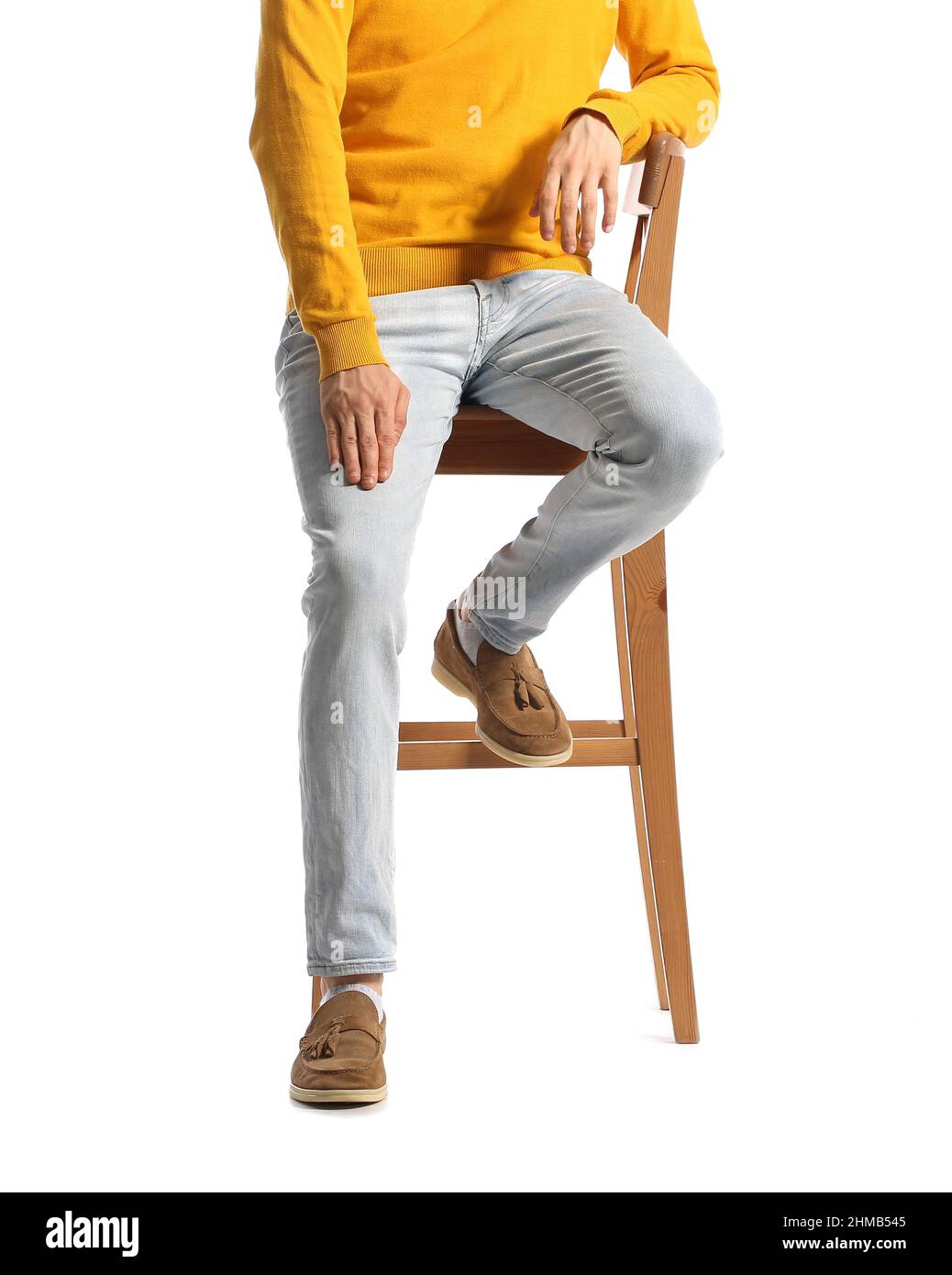 Fashionable young man in stylish jeans sitting on chair against white ...