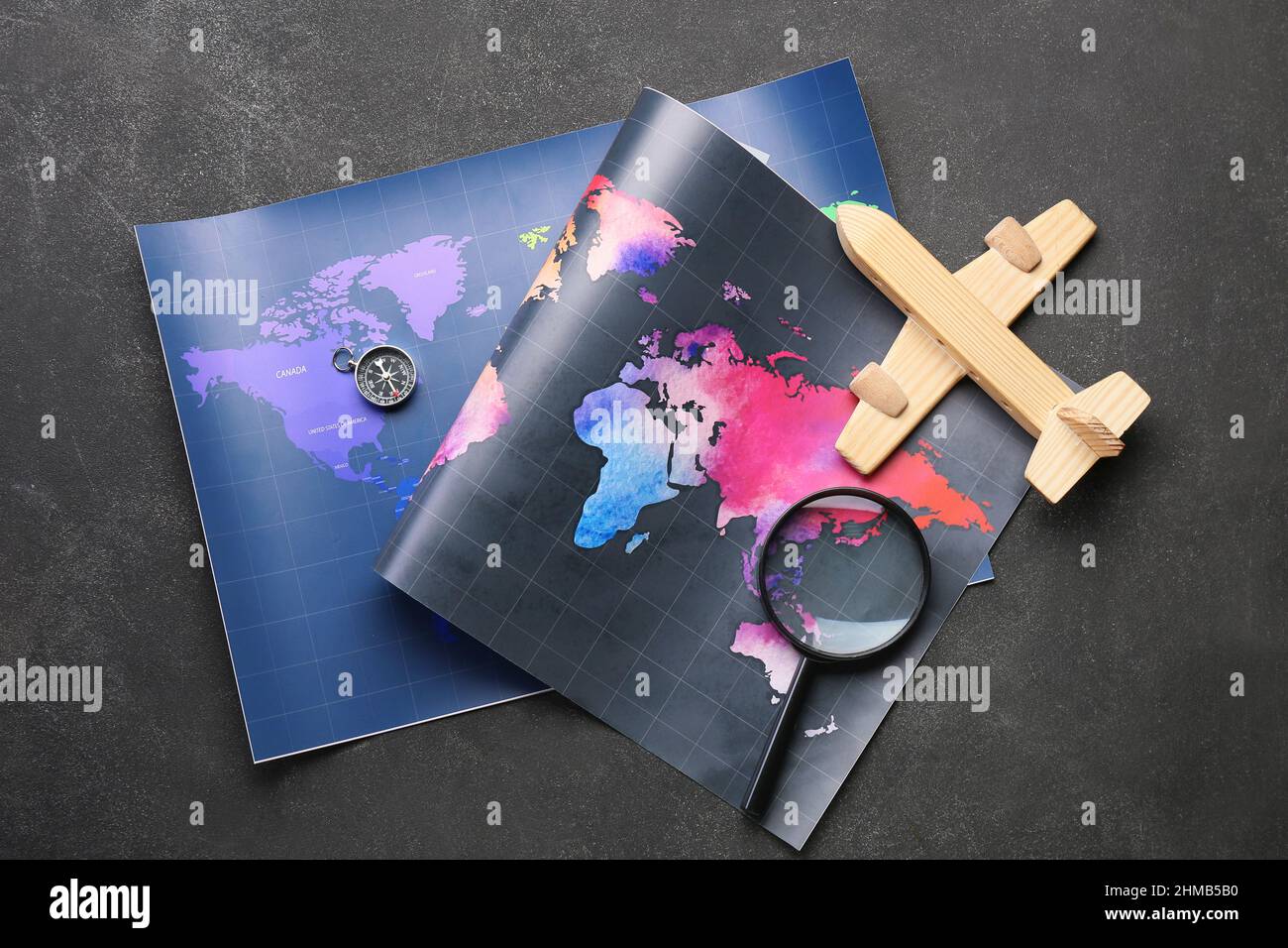 Wooden plane, magnifying glass, compass and maps on dark background ...