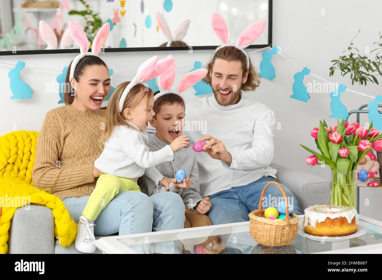 Happy family in bunny ears with Easter eggs sitting on sofa at home ...