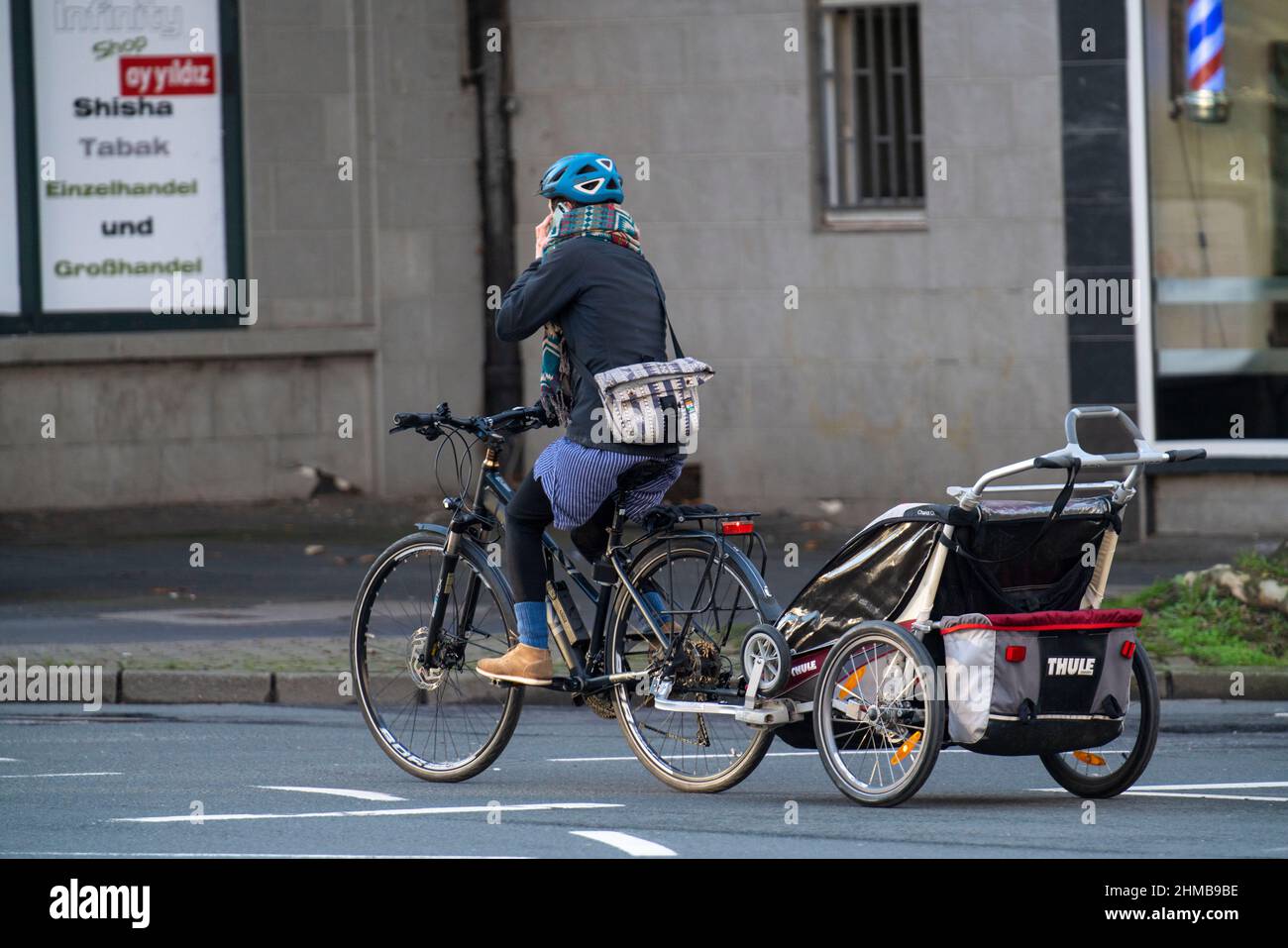 Woman riding a bicycle with a child trailer, talking on her mobile ...