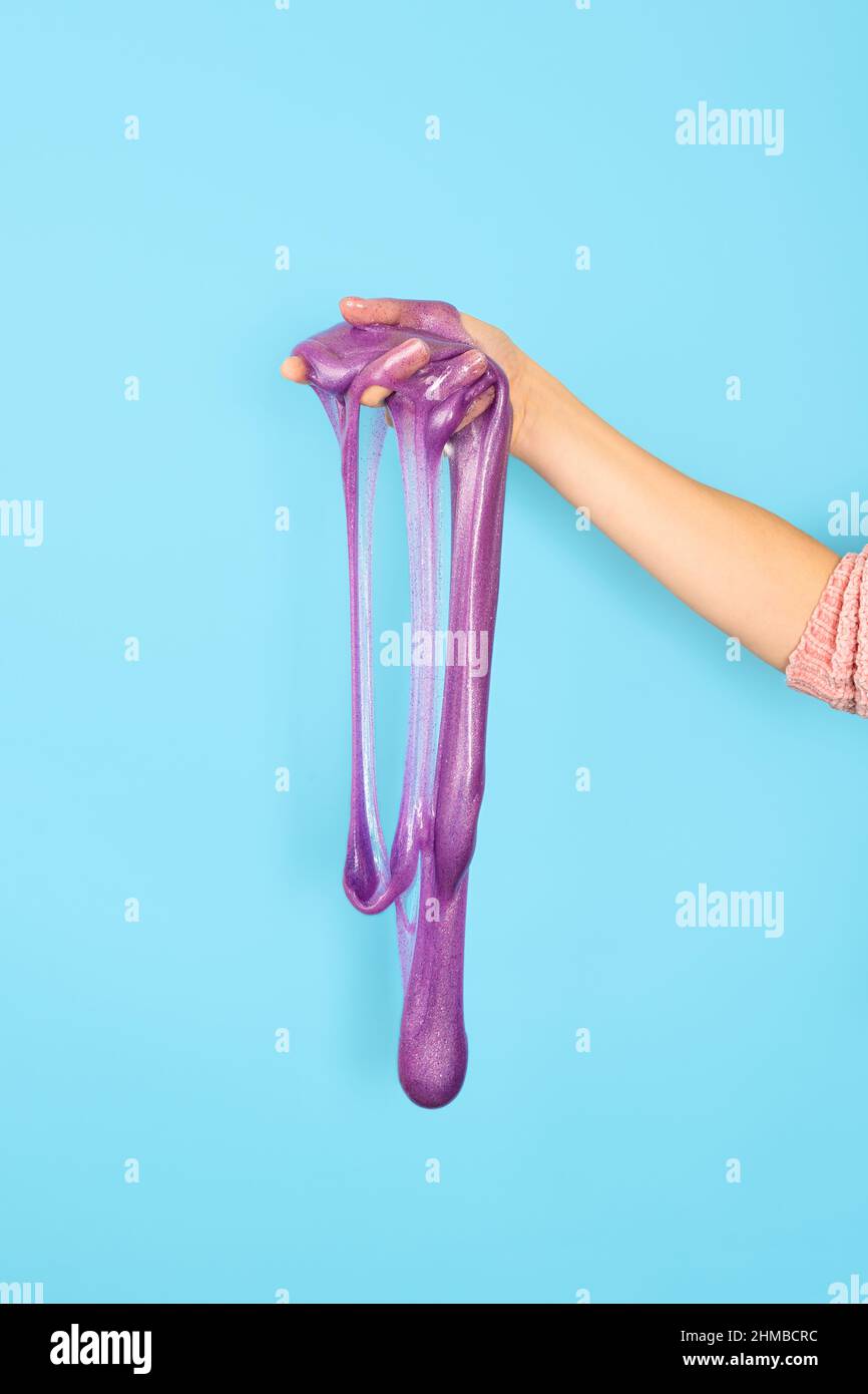 Close up on shiny purple or violet slime in the hand isolated on blue ...