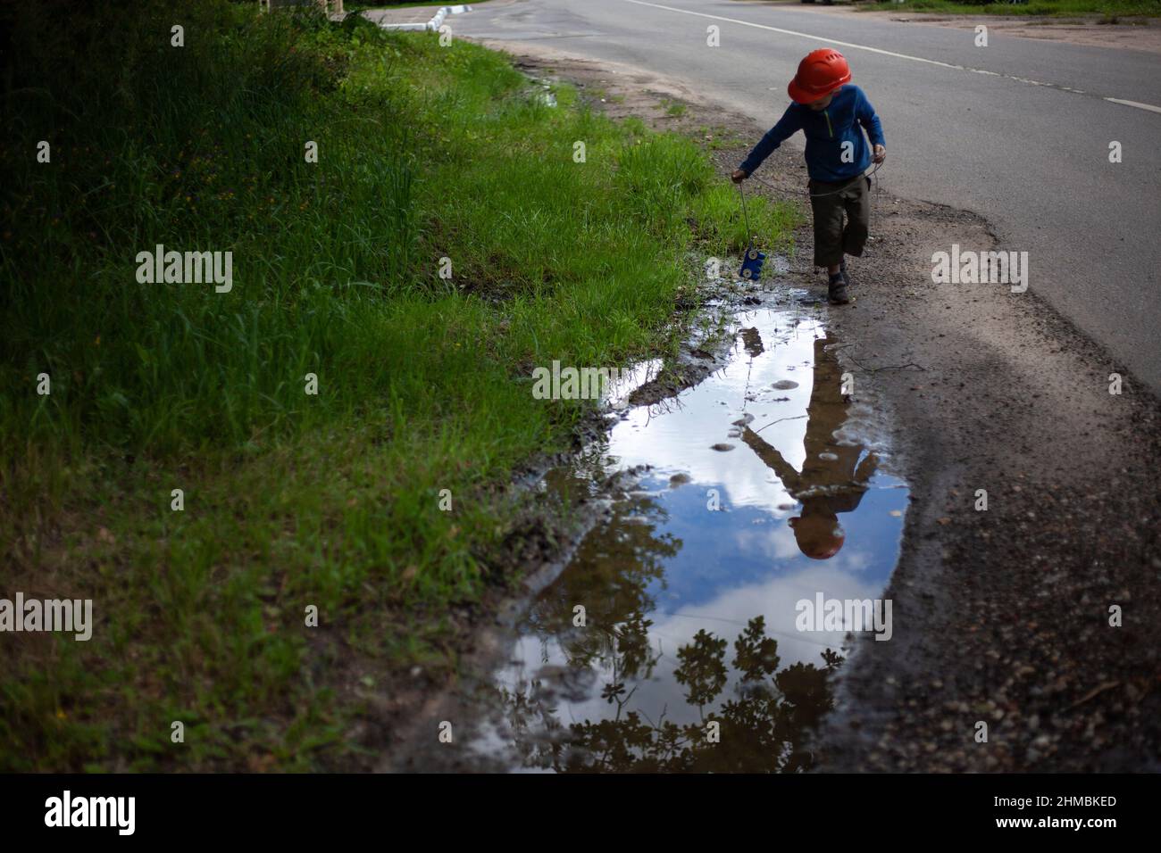 Child plays next to puddle. Boy pulls rope toy along muddy road. Child ...