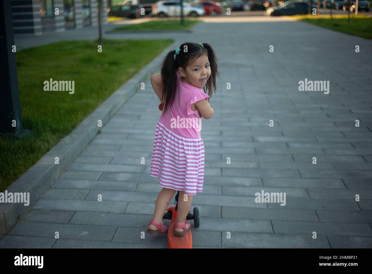 Girl on children's scooter. Child rides in park. Girl pushes to go. In ...