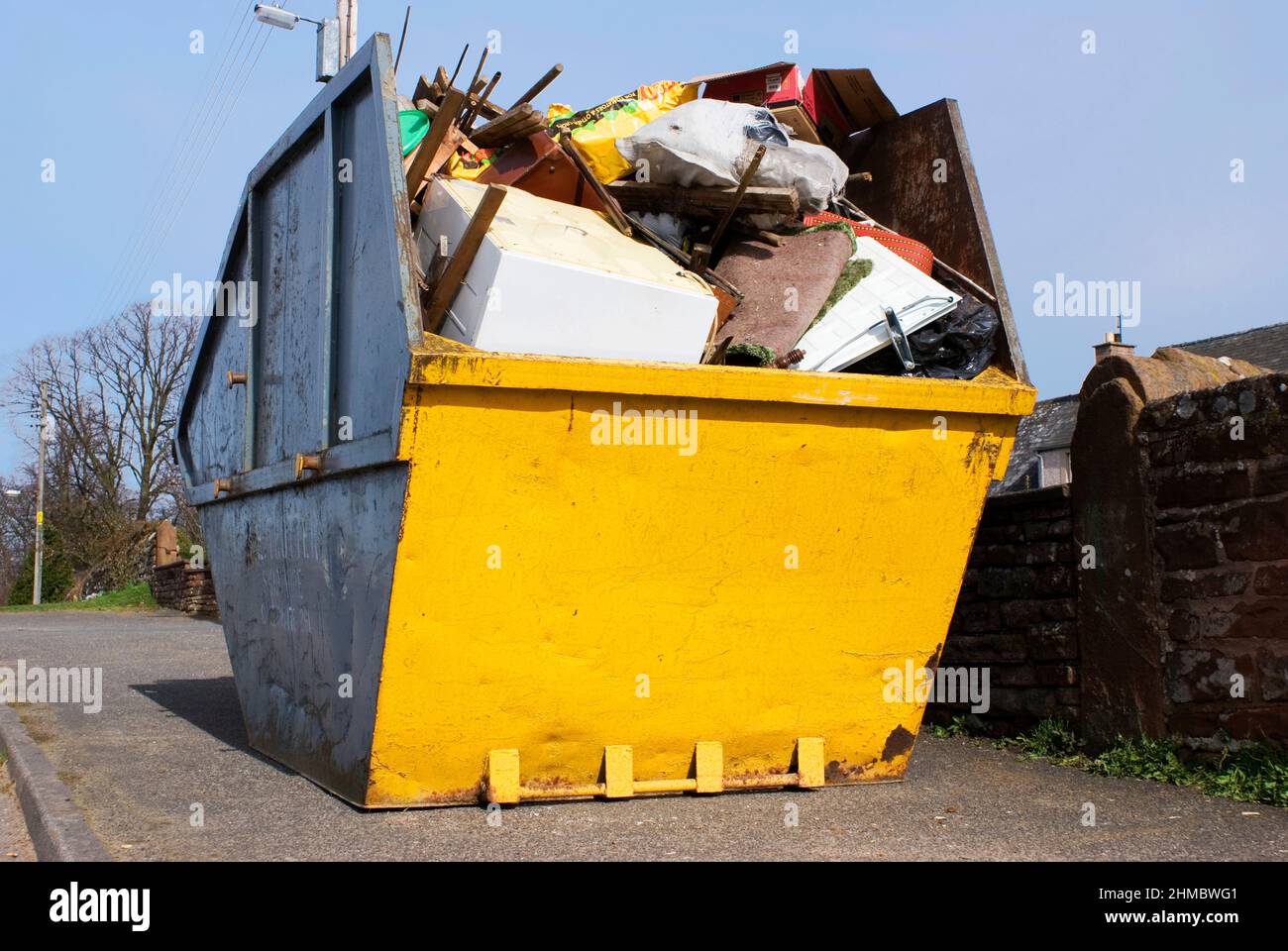 Yellow waste skip on a village street Stock Photo - Alamy