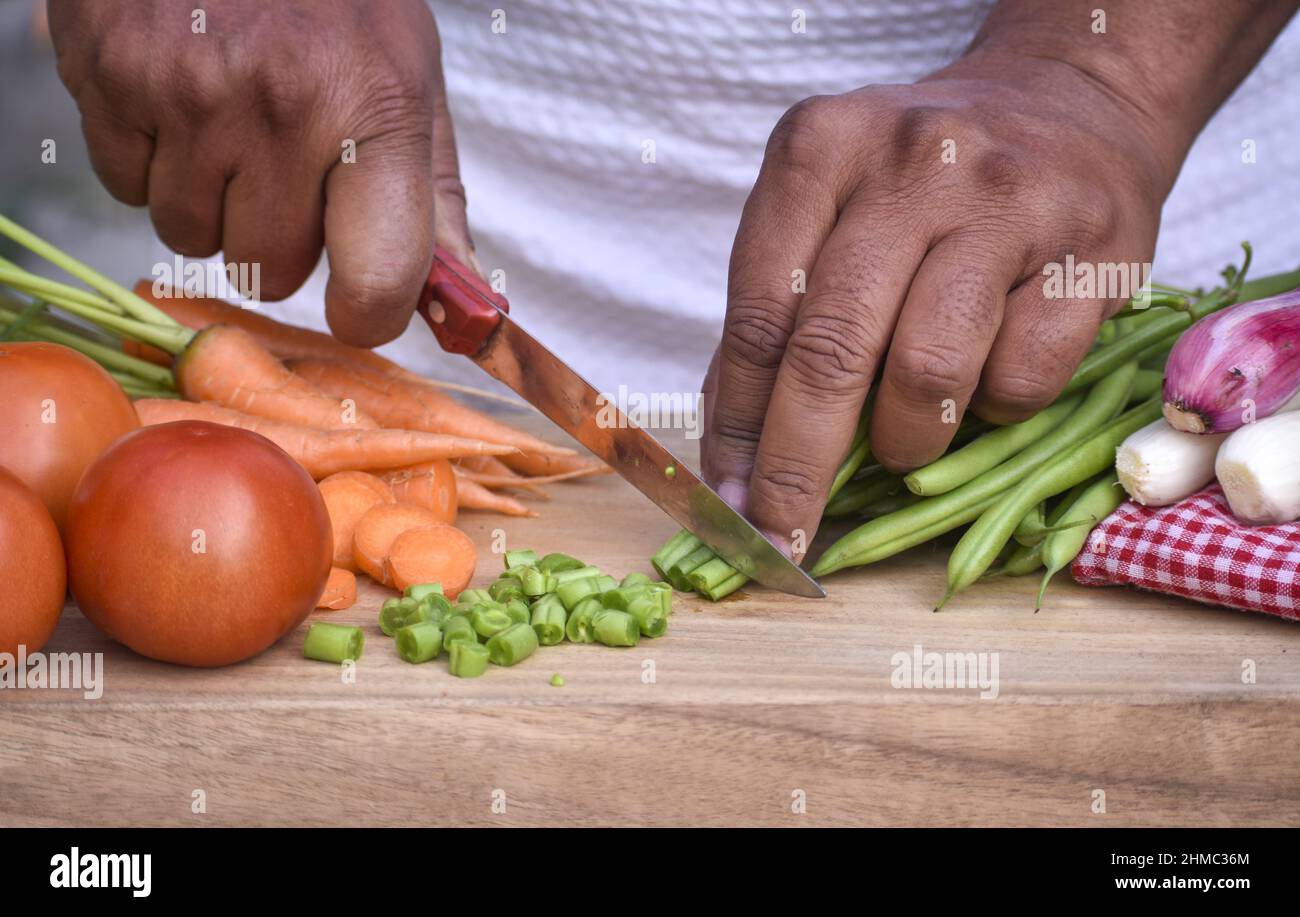 Male hands chopping vegetables on a wooden board surrounded by ...