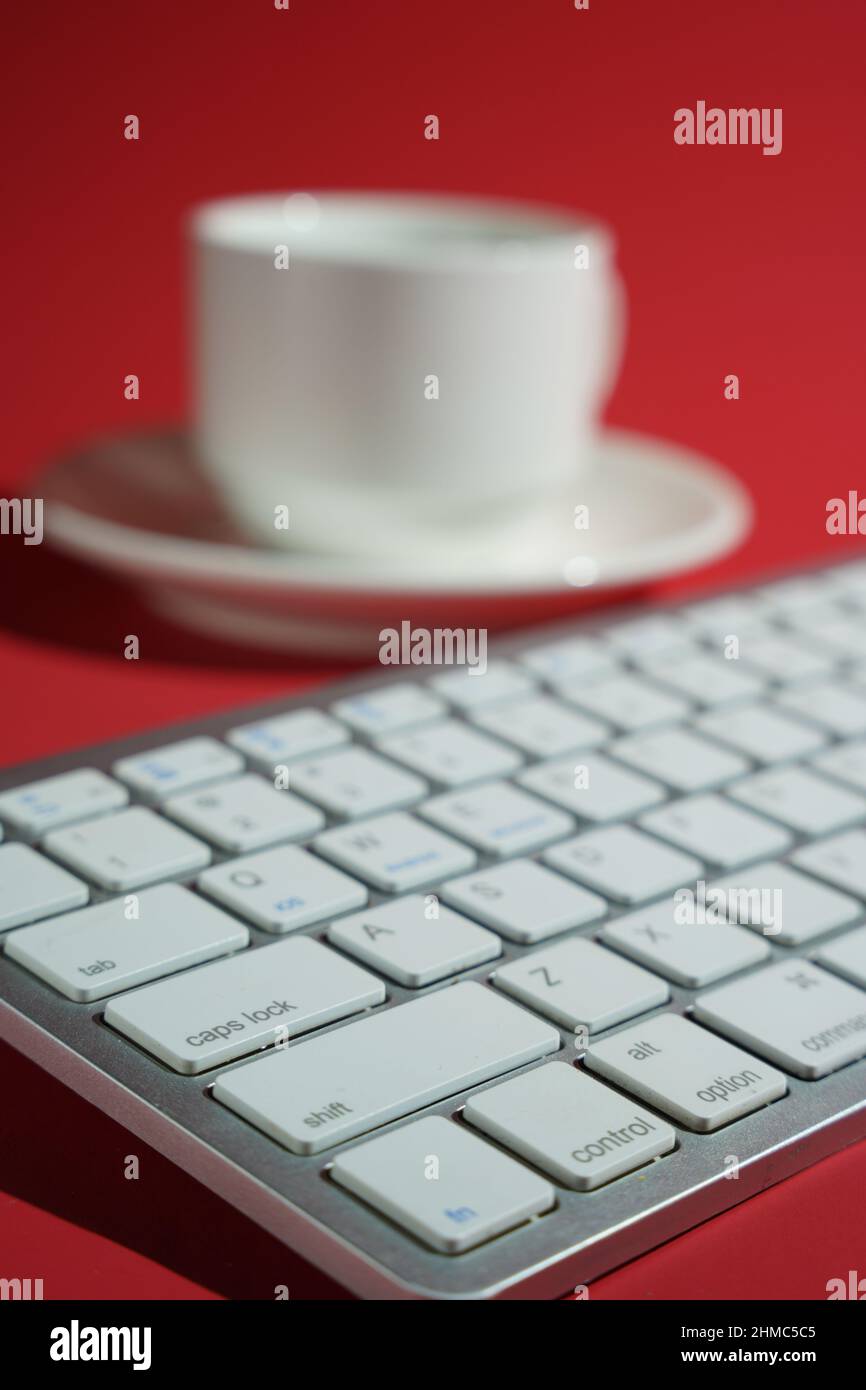 Vertical shot of a computer keyboard with a cup and saucer background ...