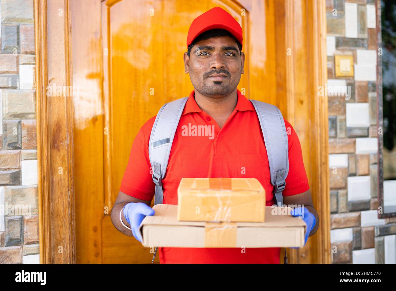 delivery boy with cardboard boxes looking at camera in front of door ...