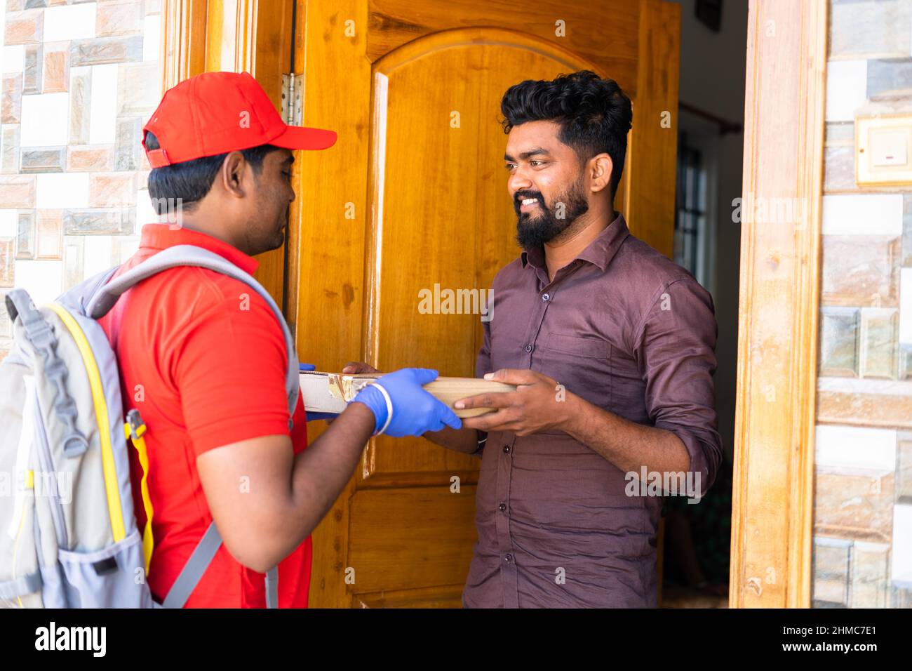 Young indian delivery boy giving parcel to consumer after opening door ...