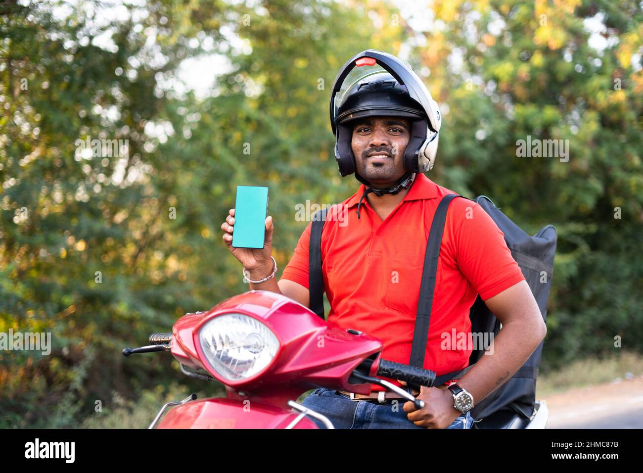 Indian happy delivery boy showing mobile phone with green screen mockup ...