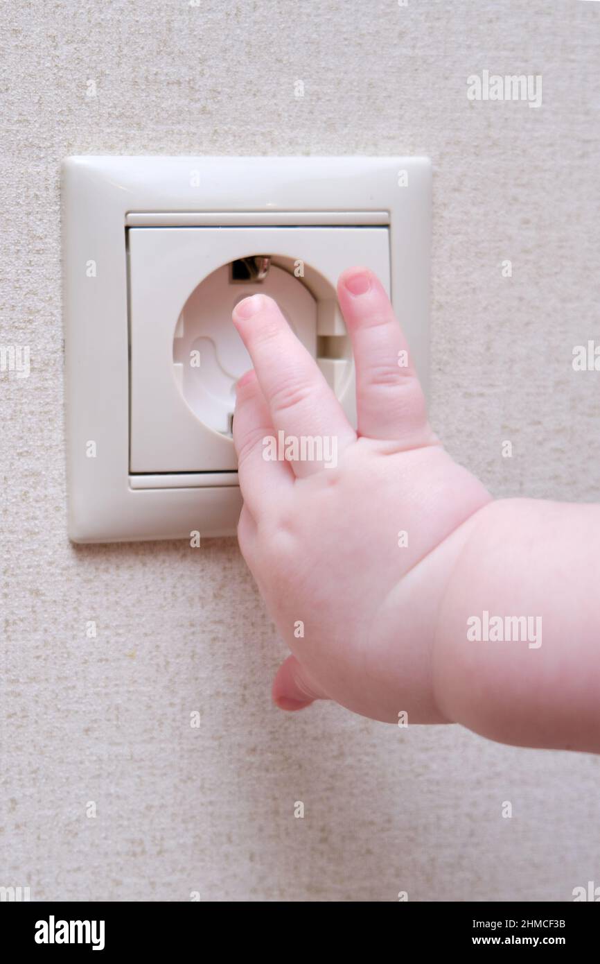 Baby toddler reaches into the electrical outlet on the home wall with ...