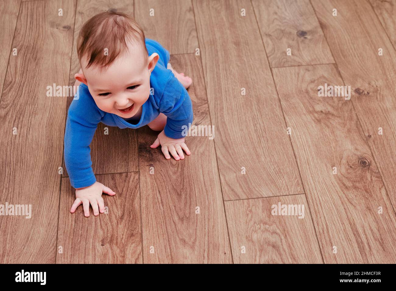 Happy baby toddler crawls on a wooden laminate. Funny child on the ...