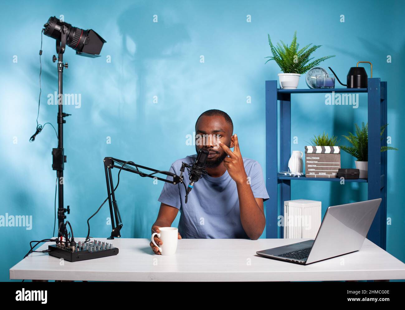 Vlogger showing peace sign sitting while holding cup at desk in ...