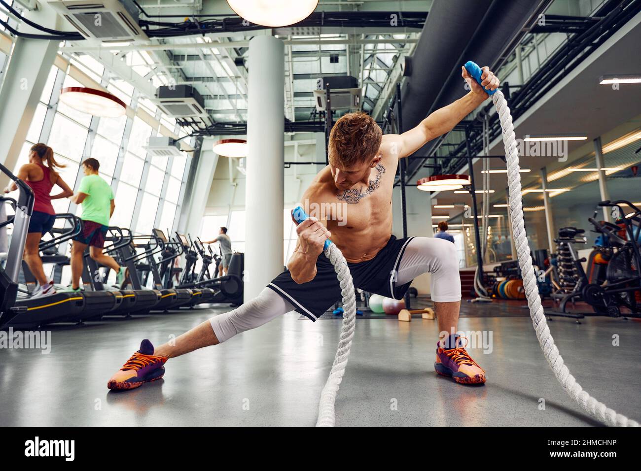 Muscular powerful aggressive man training with rope in functional ...