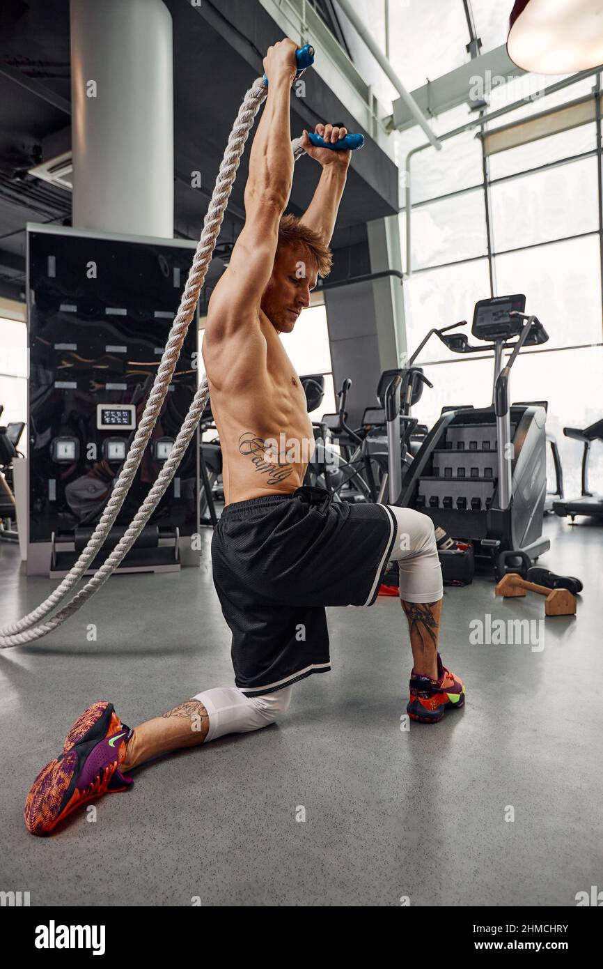 Muscular powerful aggressive man training with rope in functional ...