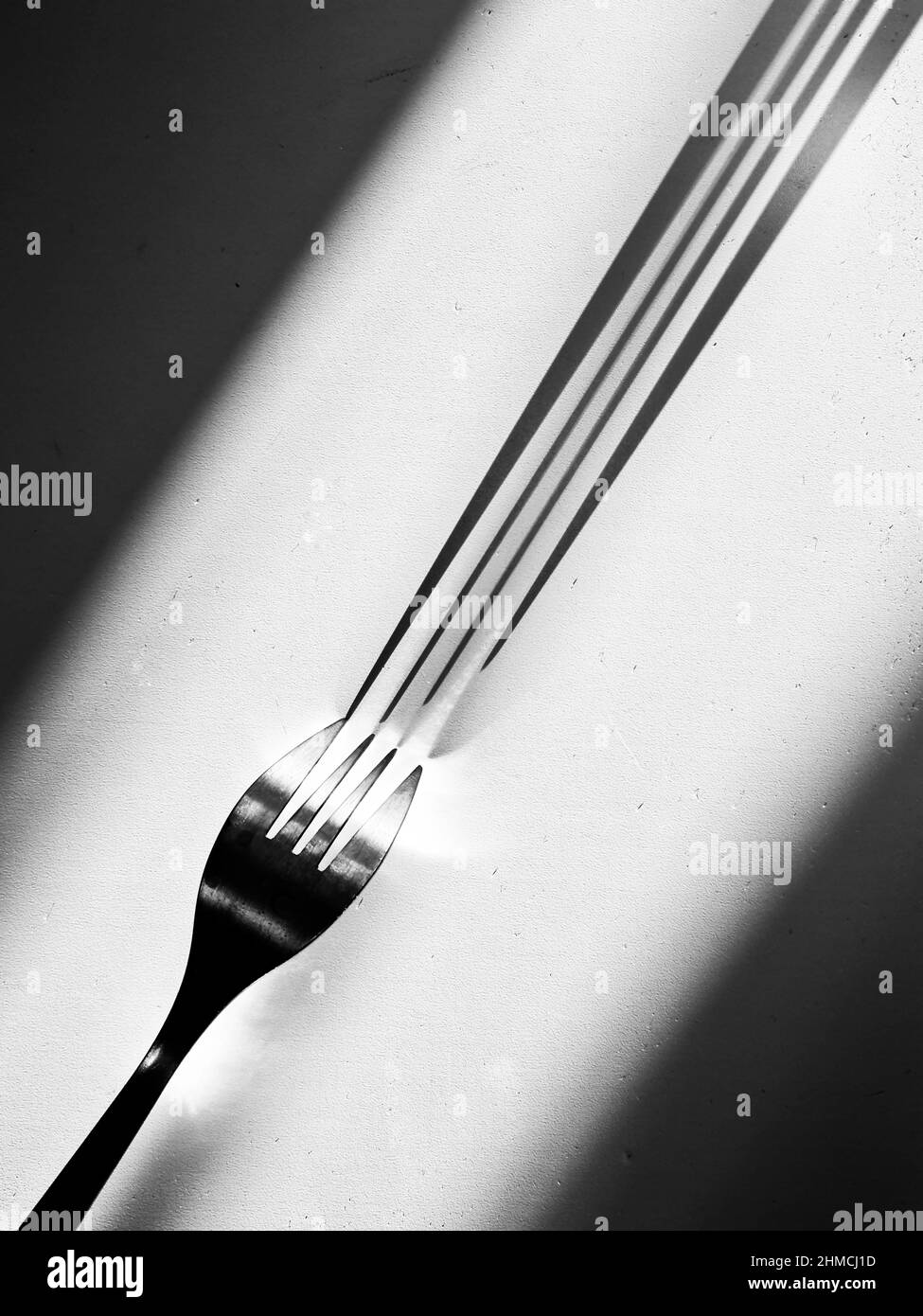 Single kitchen fork creates long shadows on a white surface Stock Photo ...