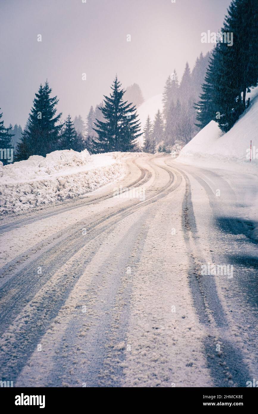 Snowy and icy road along a hill slope in bad weather with glance of sun ...