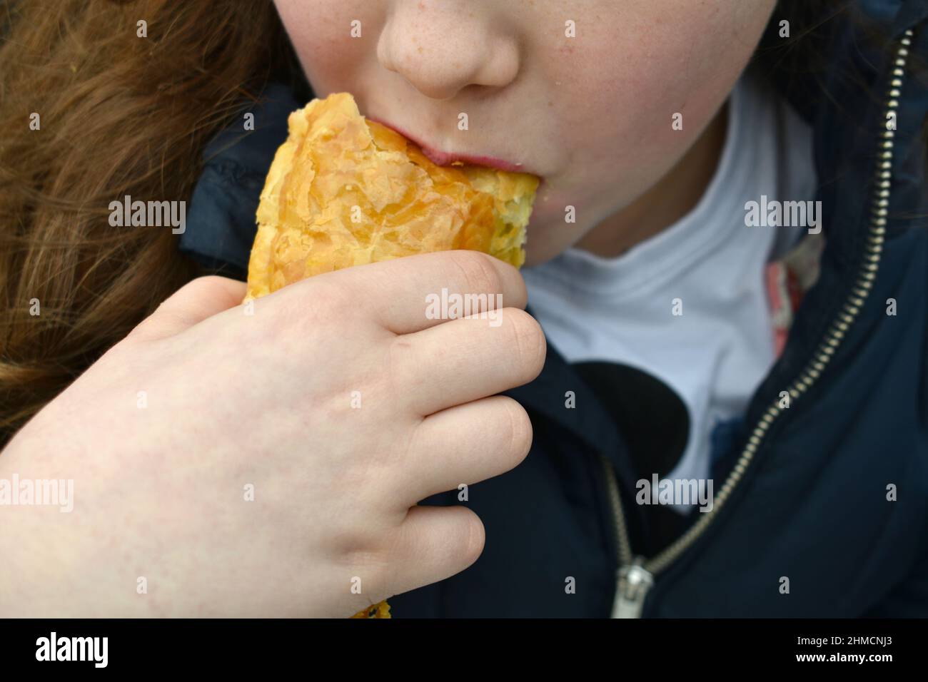close up of young girl's mouth taking a bite from a pastry snack. The ...