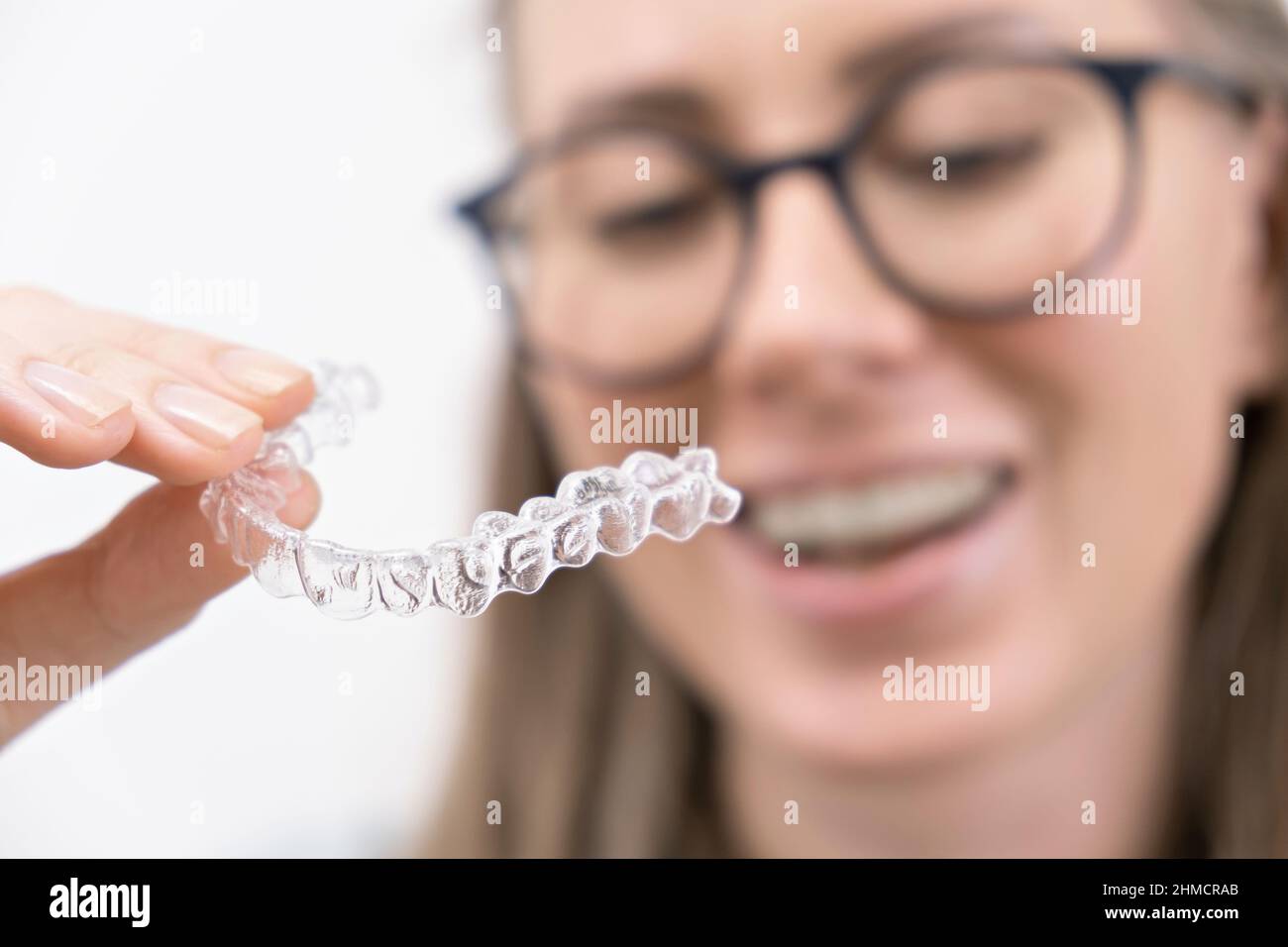 smiling woman using clear plastic removable braces aligner or whitening ...