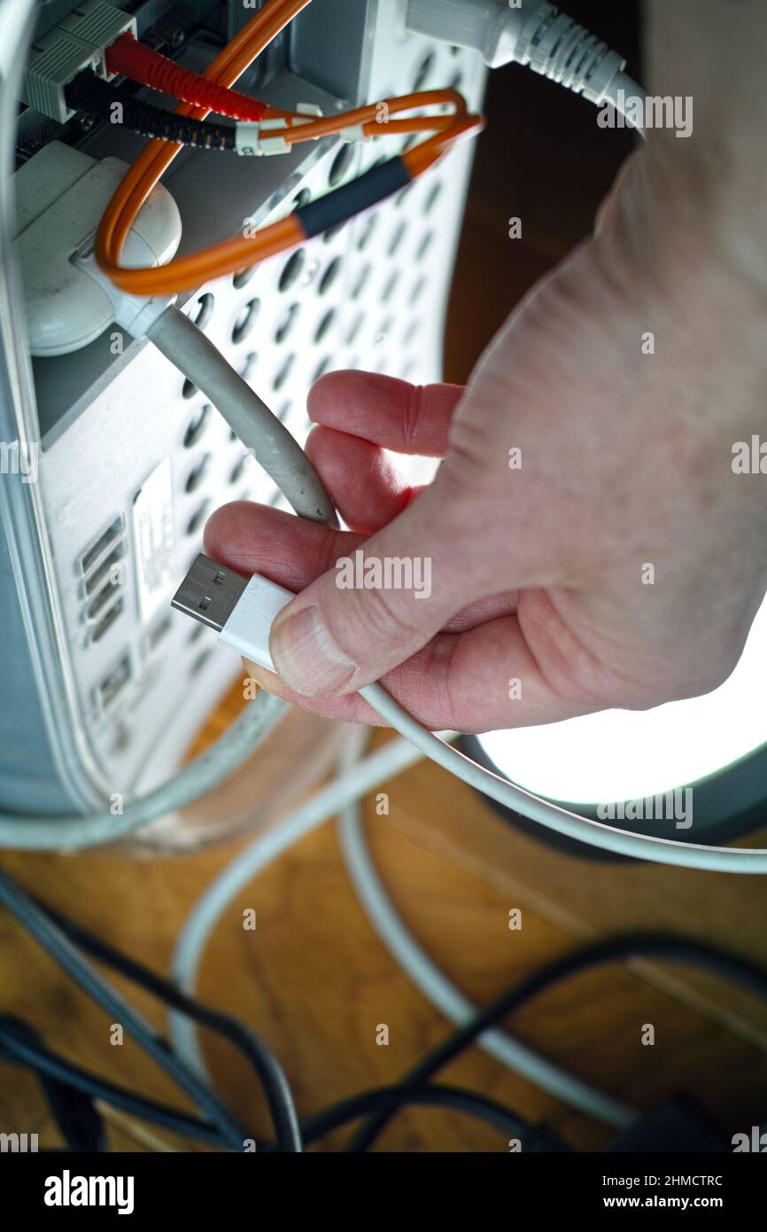 a hand plugging usb cable into a rear of old computer, vertical closeup ...