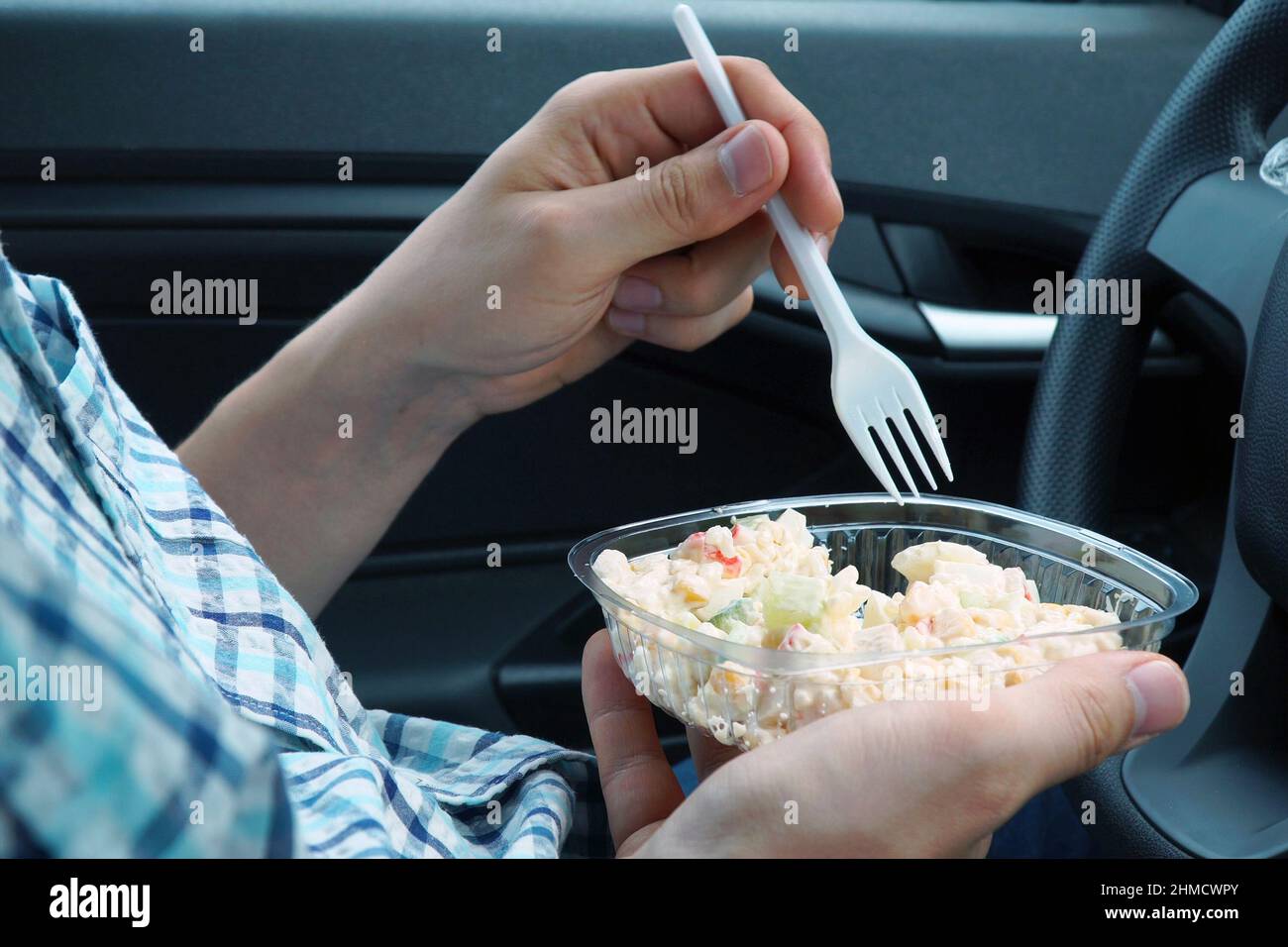 A man, sitting in a car, eats a salad with mayonnaise from plastic ...