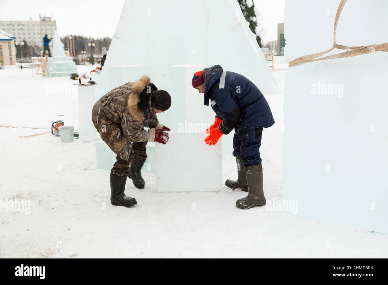 Workers in winter overalls carry an ice block on their hands at a ...