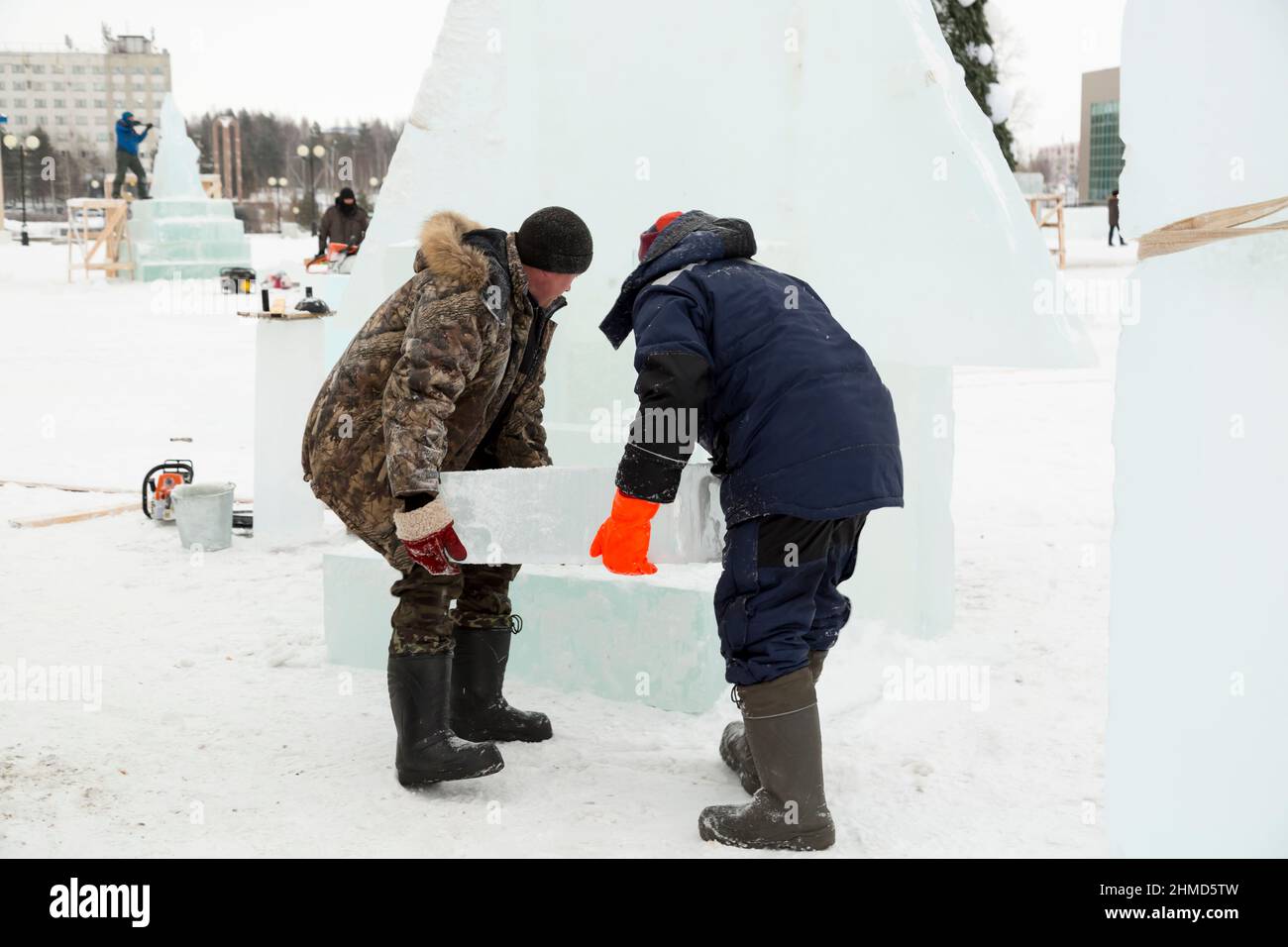 Workers in winter overalls carry an ice block on their hands at a ...