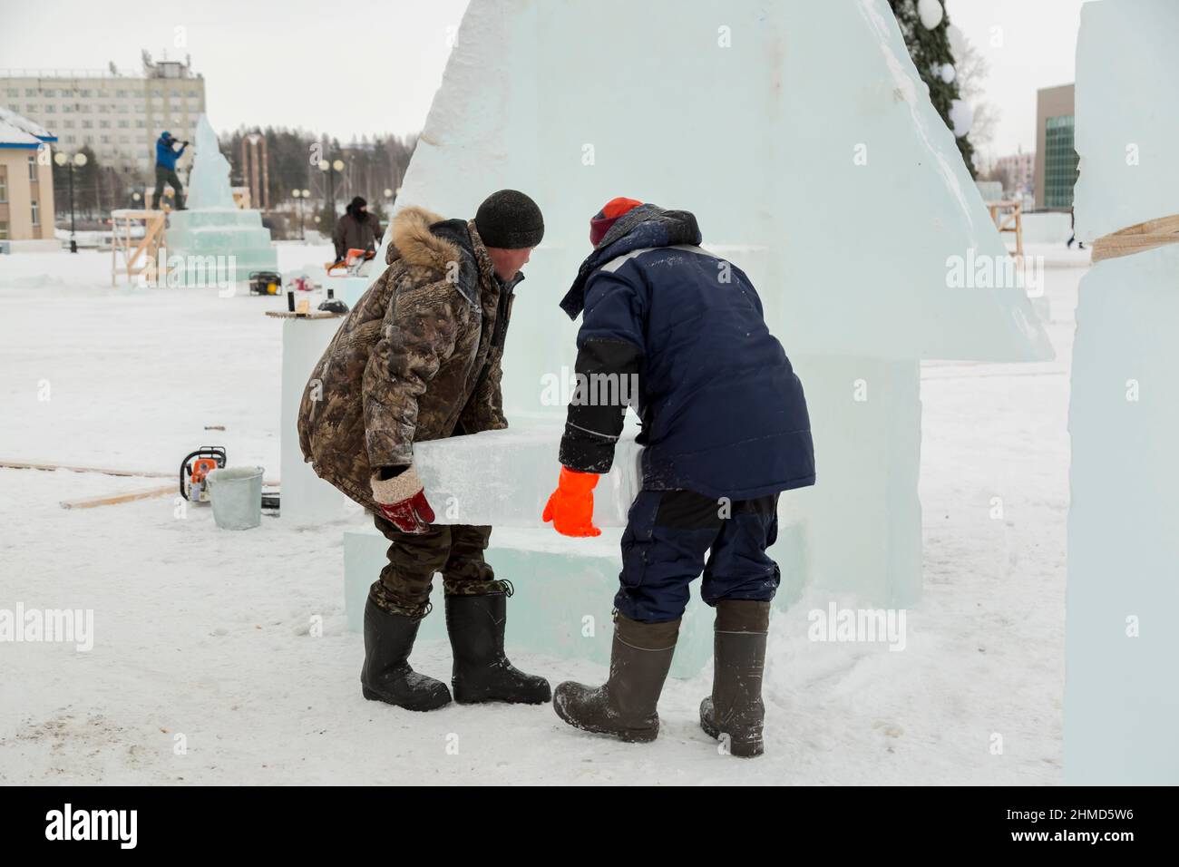 Workers in winter overalls carry an ice block on their hands at a ...