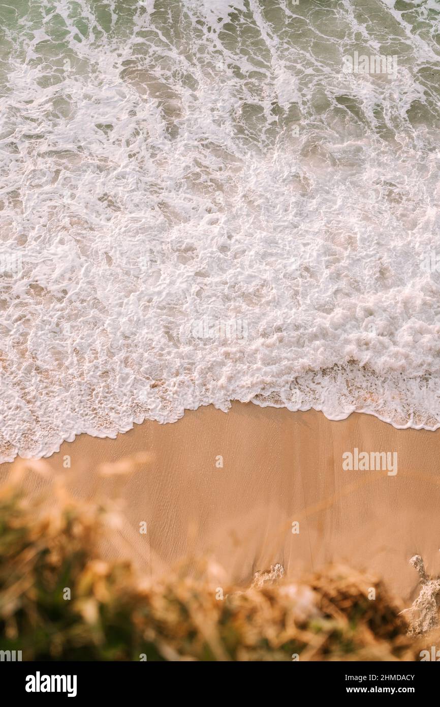 Vertical top view of the ocean waves meeting sandy beach and rocks ...