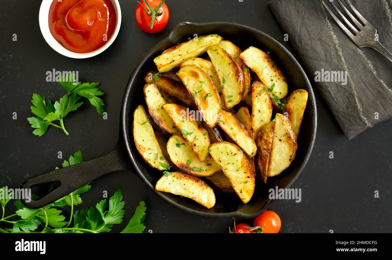 Homemade fried potato wedges in frying pan over black stone background ...
