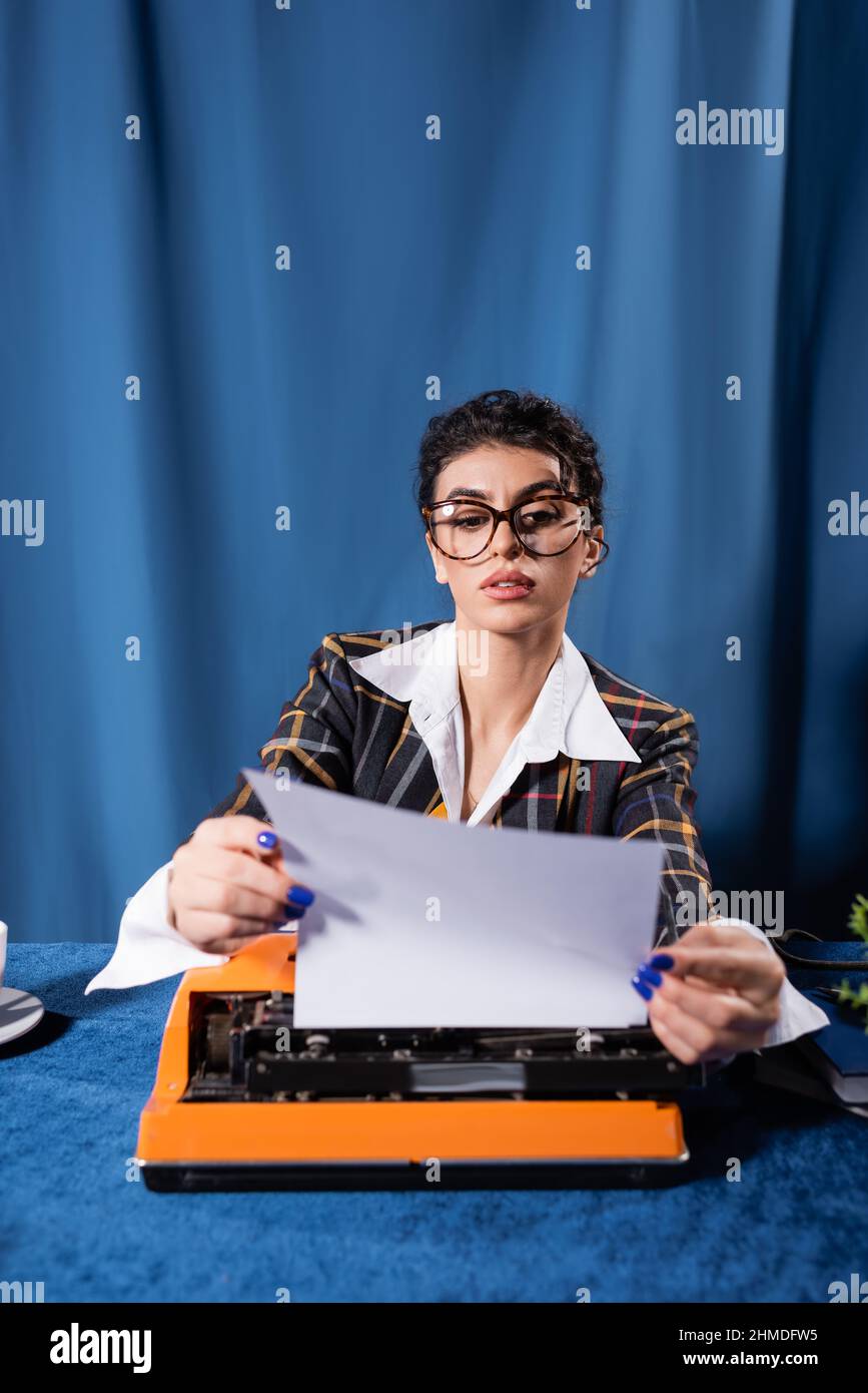 journalist in vintage style clothes holding empty paper near typewriter ...