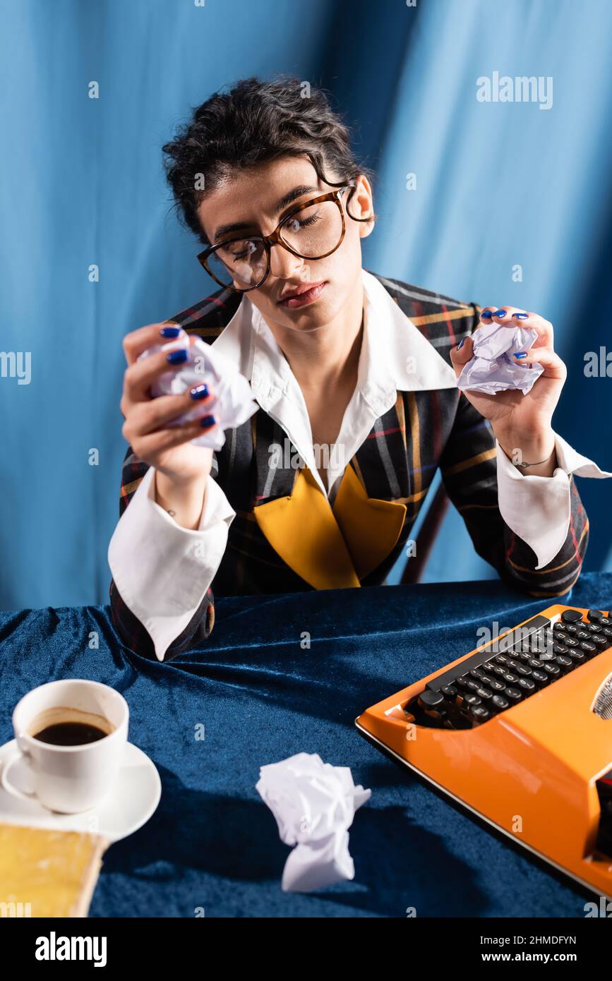 upset and exhausted journalist holding crumpled paper near typewriter ...