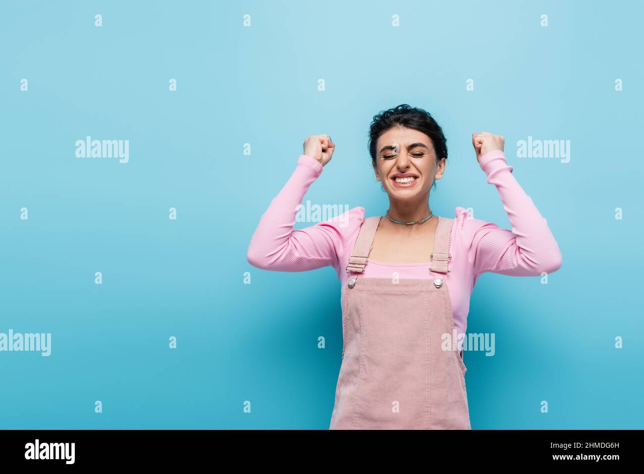 overjoyed woman showing yeah gesture while standing with closed eyes ...