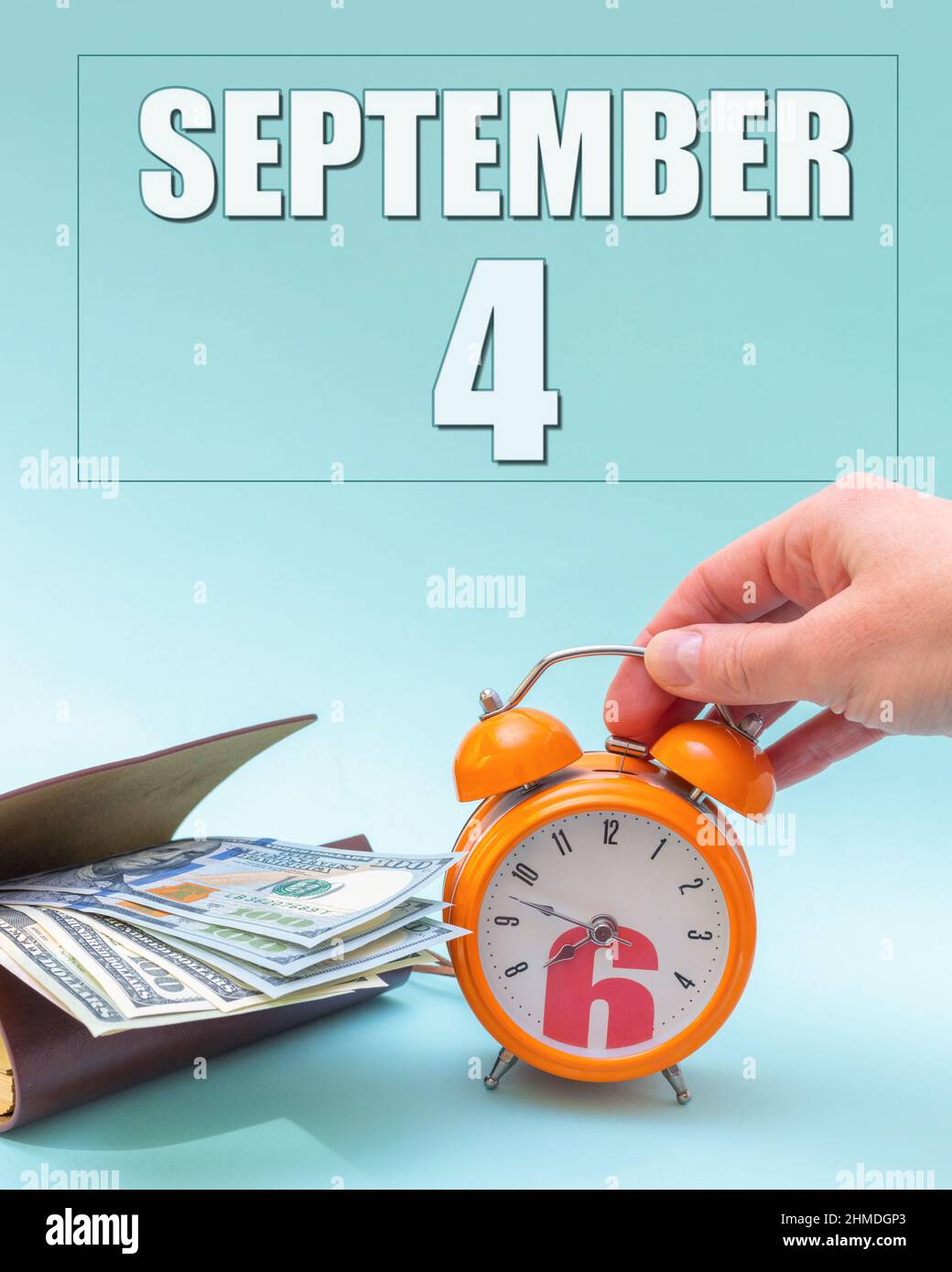September 4th. Hand holding an orange alarm clock, a wallet with cash ...